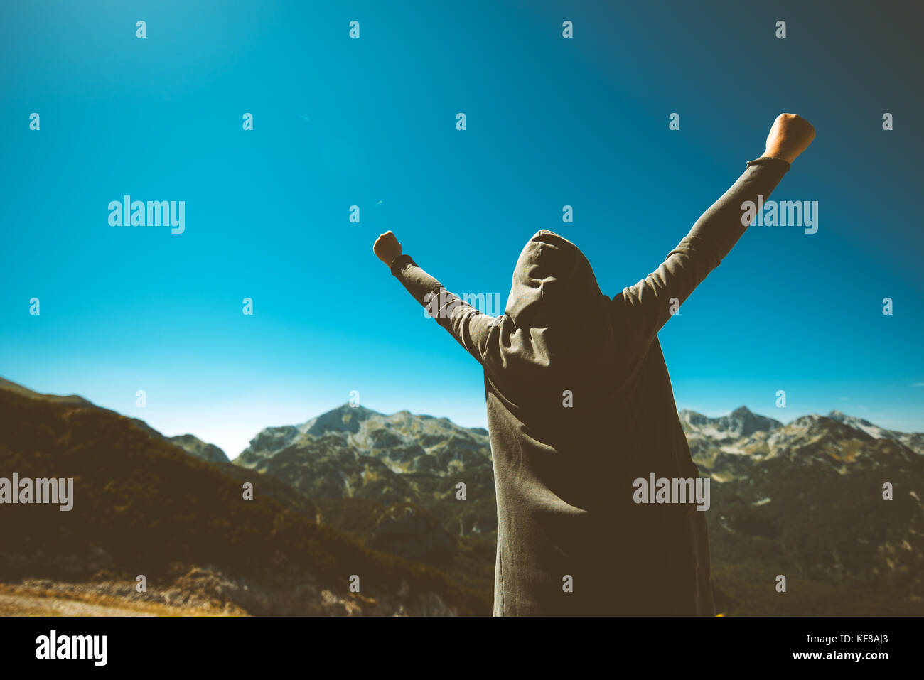 Victorious female person standing on mountain top with arms raised in V ...