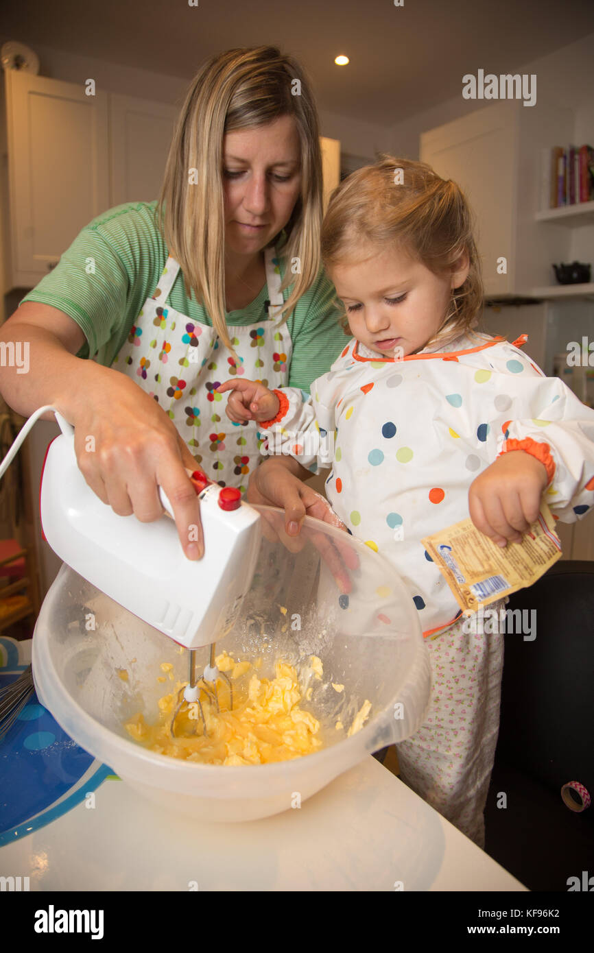 Mother and daughter mixing ingredients in preparation for baking a cake ...