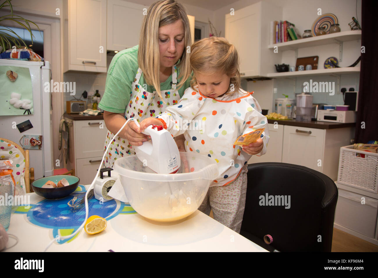 Mother and daughter mixing ingredients in preparation for baking a cake ...