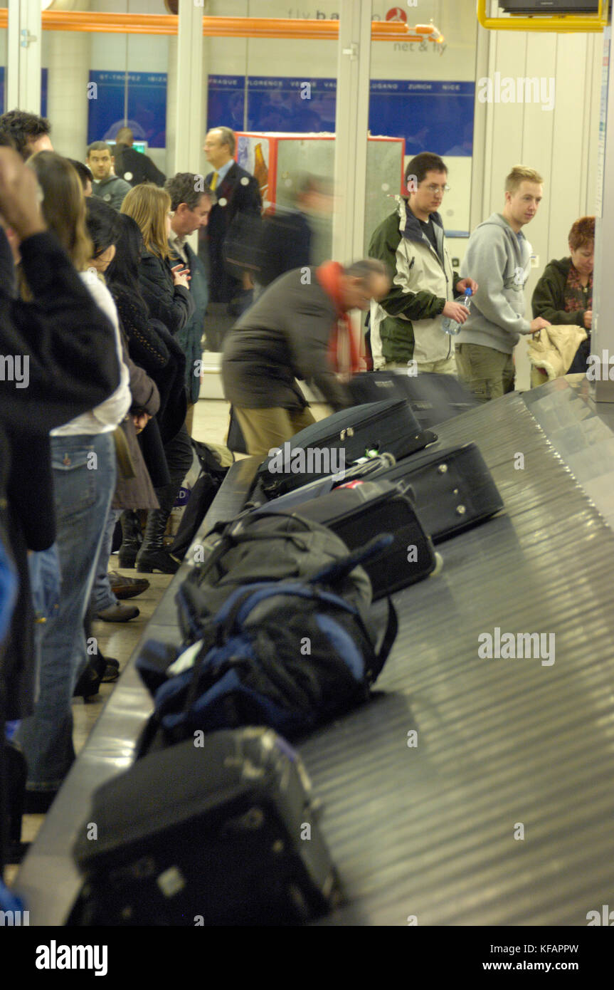 passengers standing waiting, with bags on the carousel in the arrivals ...