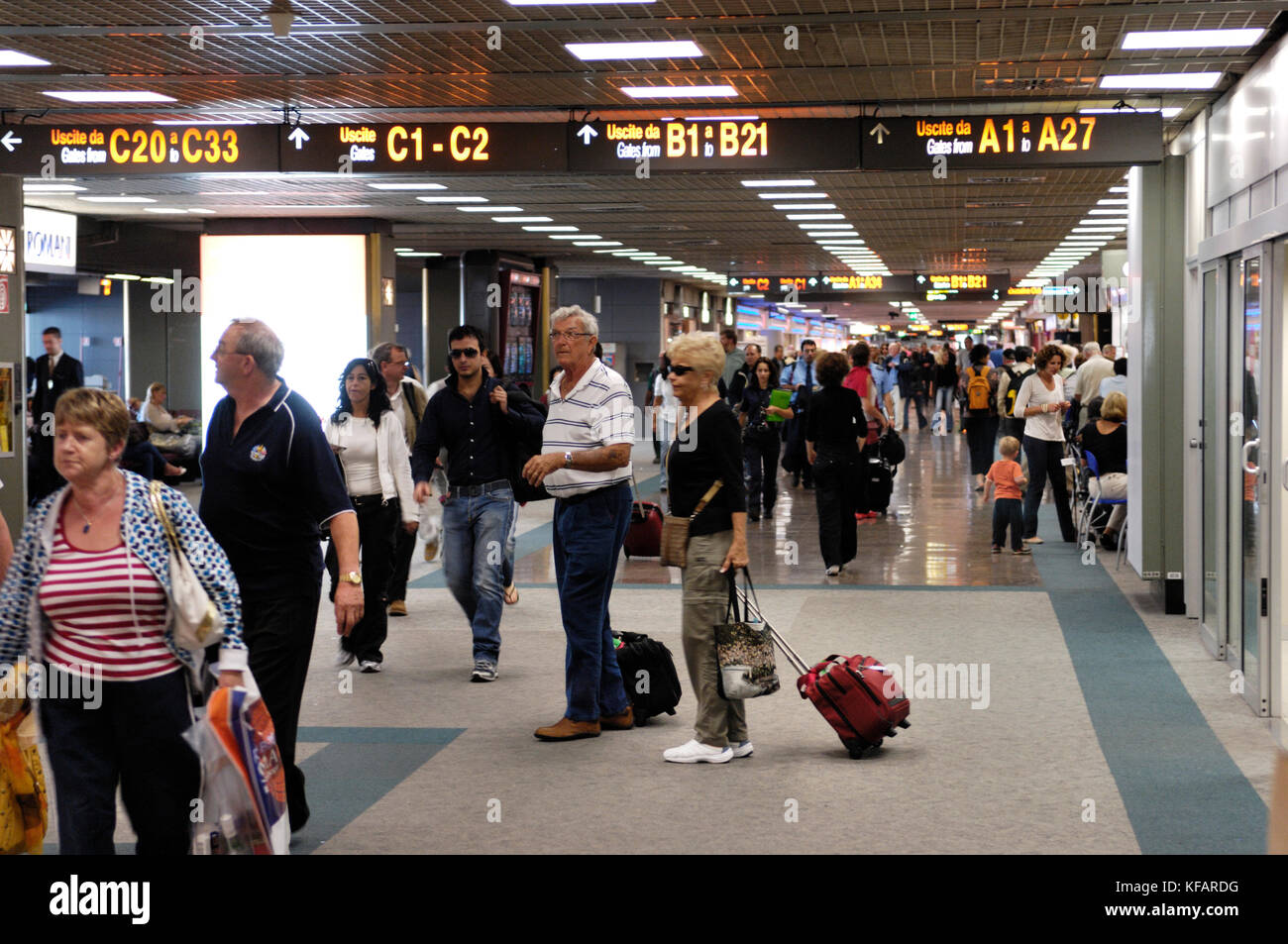 passengers with wheellie-bags walking in the terminal with signs for ...