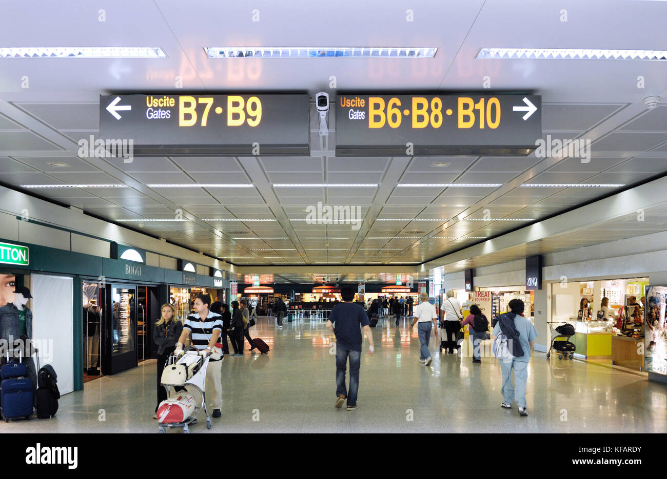 passengers walking with baggage past the shops in the terminal under ...