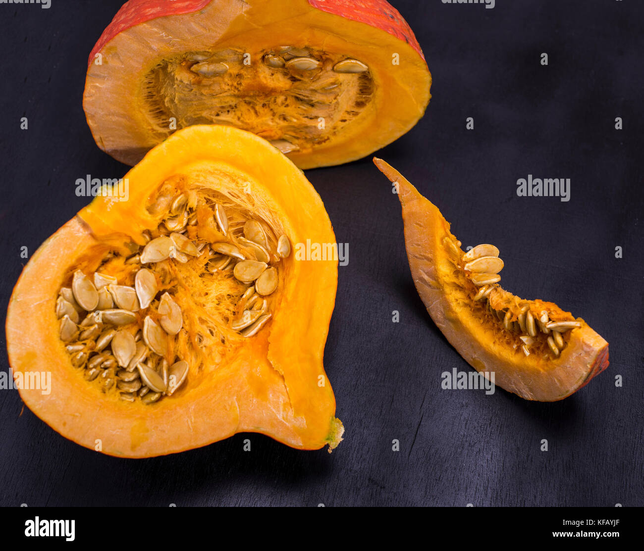 fresh pumpkin with seeds cut in half on a black background, close up ...