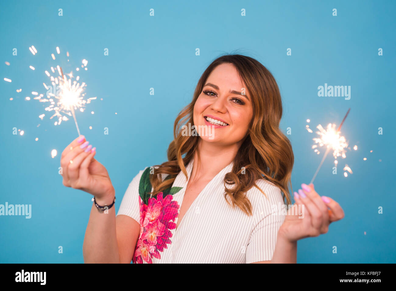 Happy woman having fun with a sparkler on blue background with ...