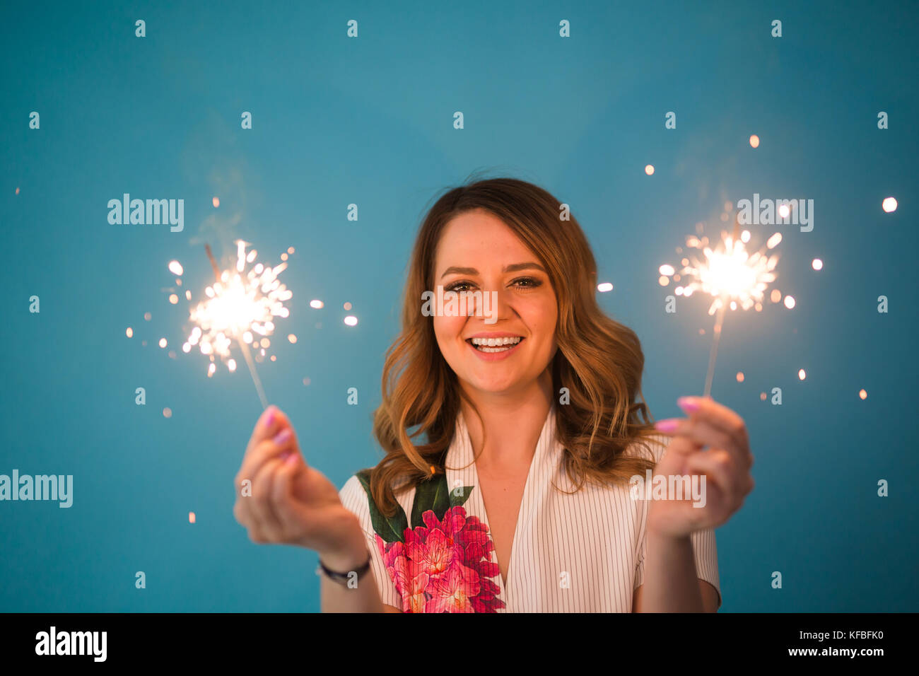 Happy woman having fun with a sparkler on blue background with ...