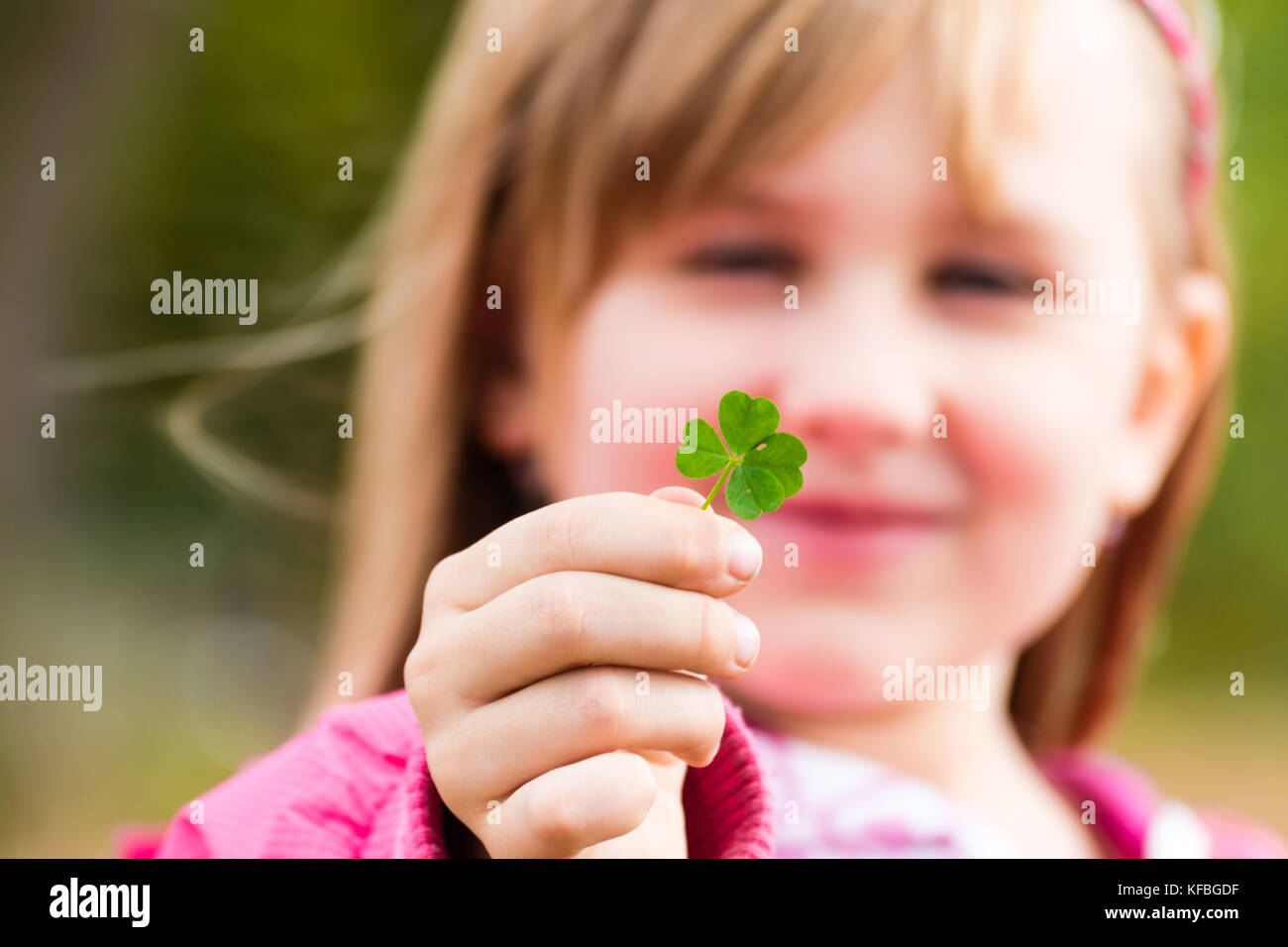 Four leaf clover in small hand of young girl in front of her face. Girl ...