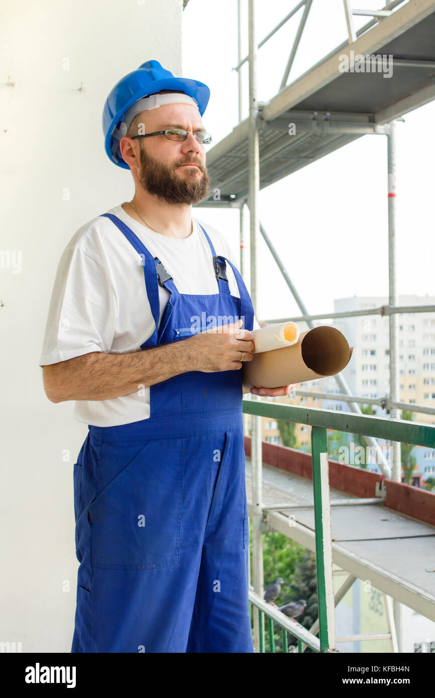 construction worker in a work outfit and in a helmet stands at a high ...