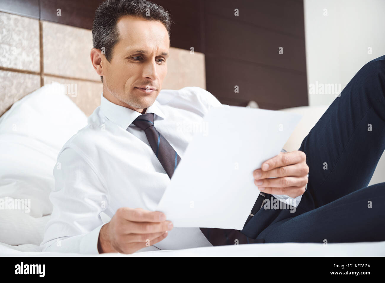 Businessman on bed reading paperwork Stock Photo - Alamy