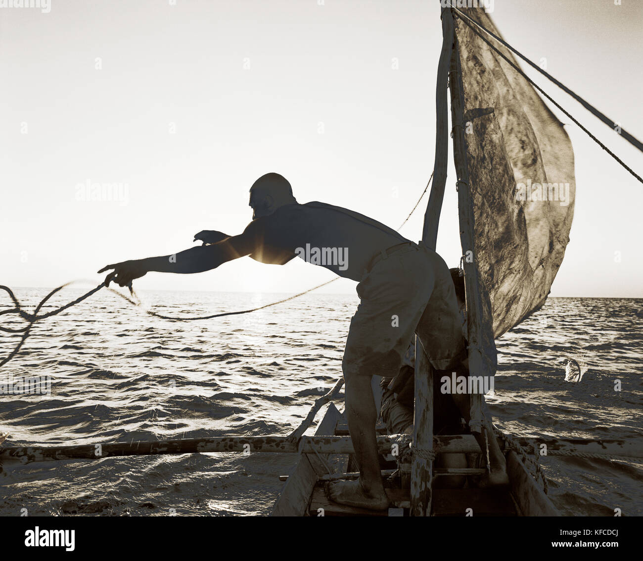 MADAGASCAR, Anjajavy, fisherman in pirogue throwing a rope at dusk ...