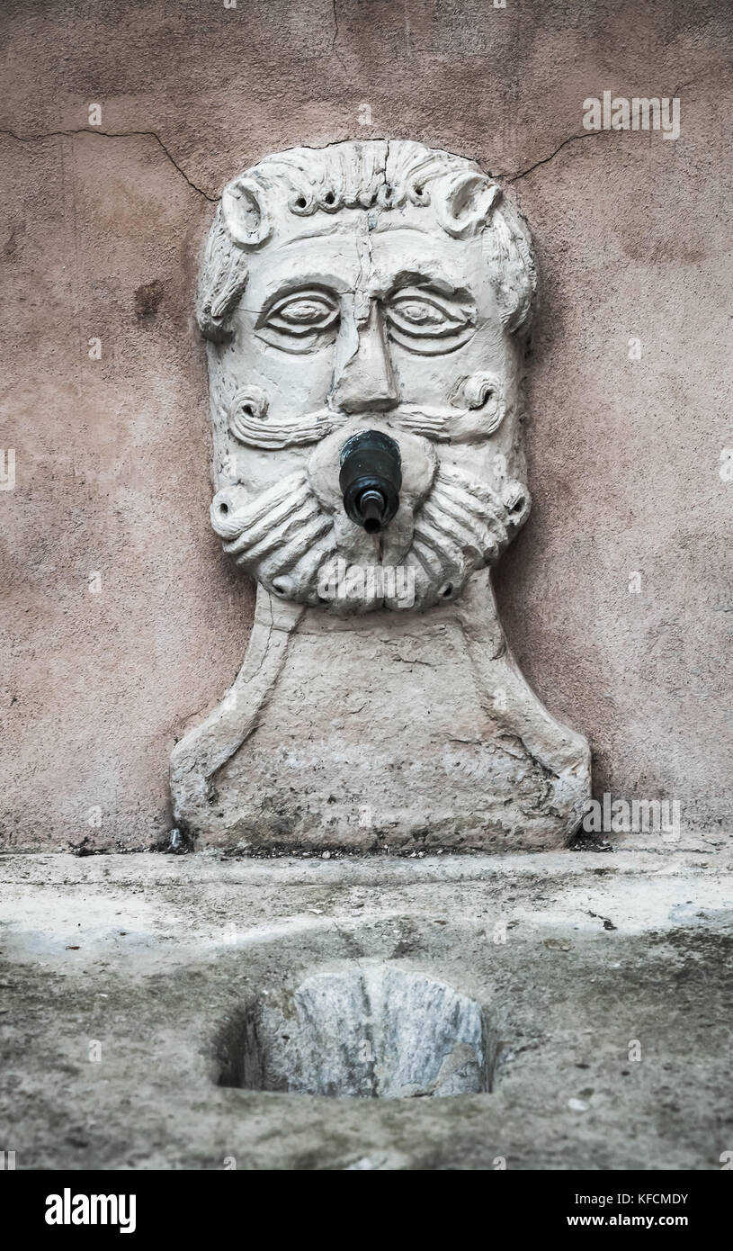 Ancient fountain with drinking water in the shape of a male face. Fermo ...