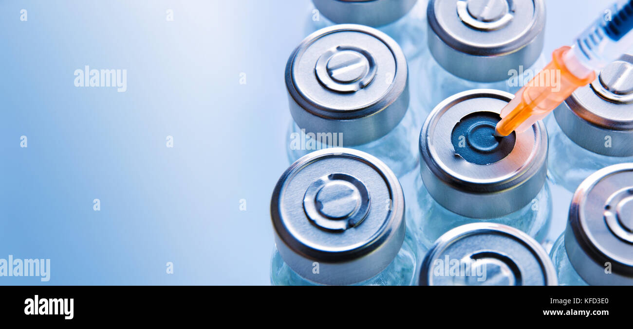 Group of vials with medication and punctured syringe on blue ...