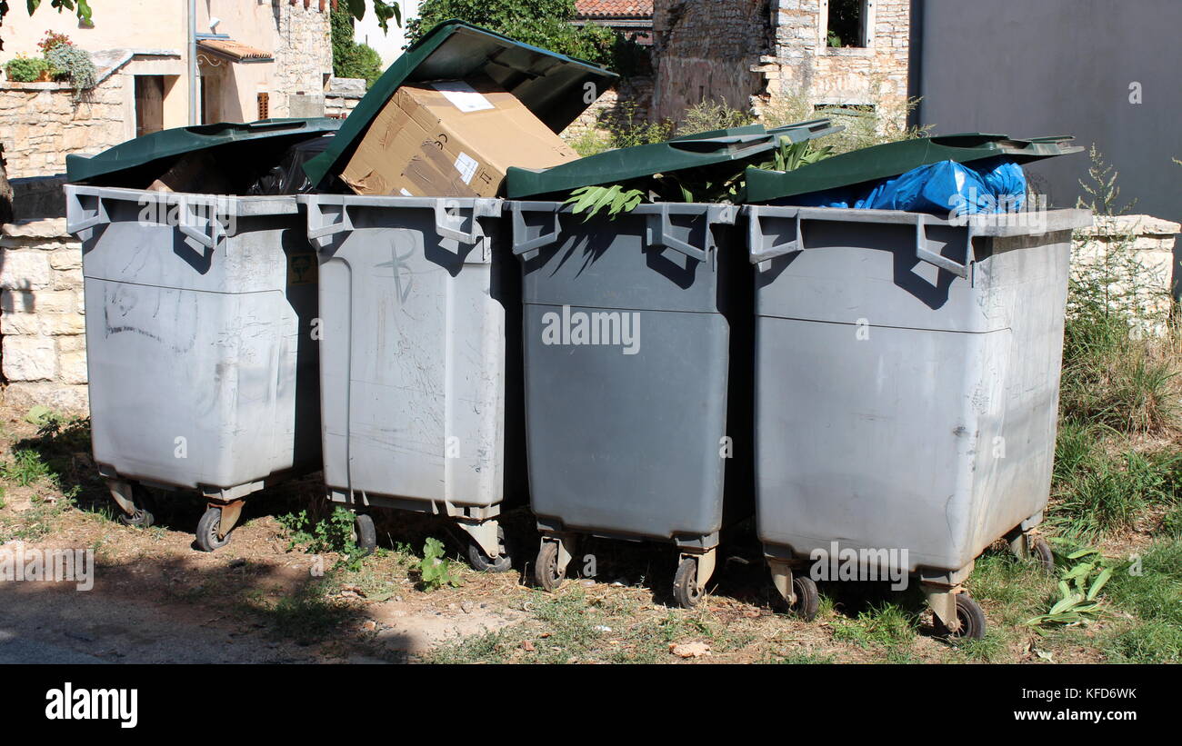 Completely full partially open four gray plastic trash containers with ...