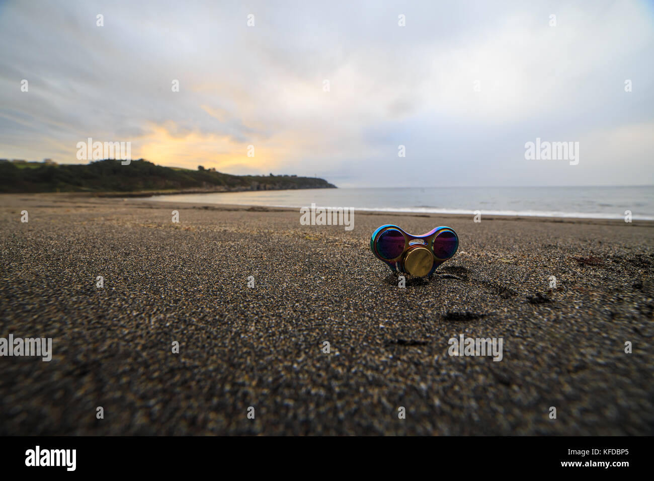 Metal fidget spinner stuck into wet sand on background of sea and beach ...