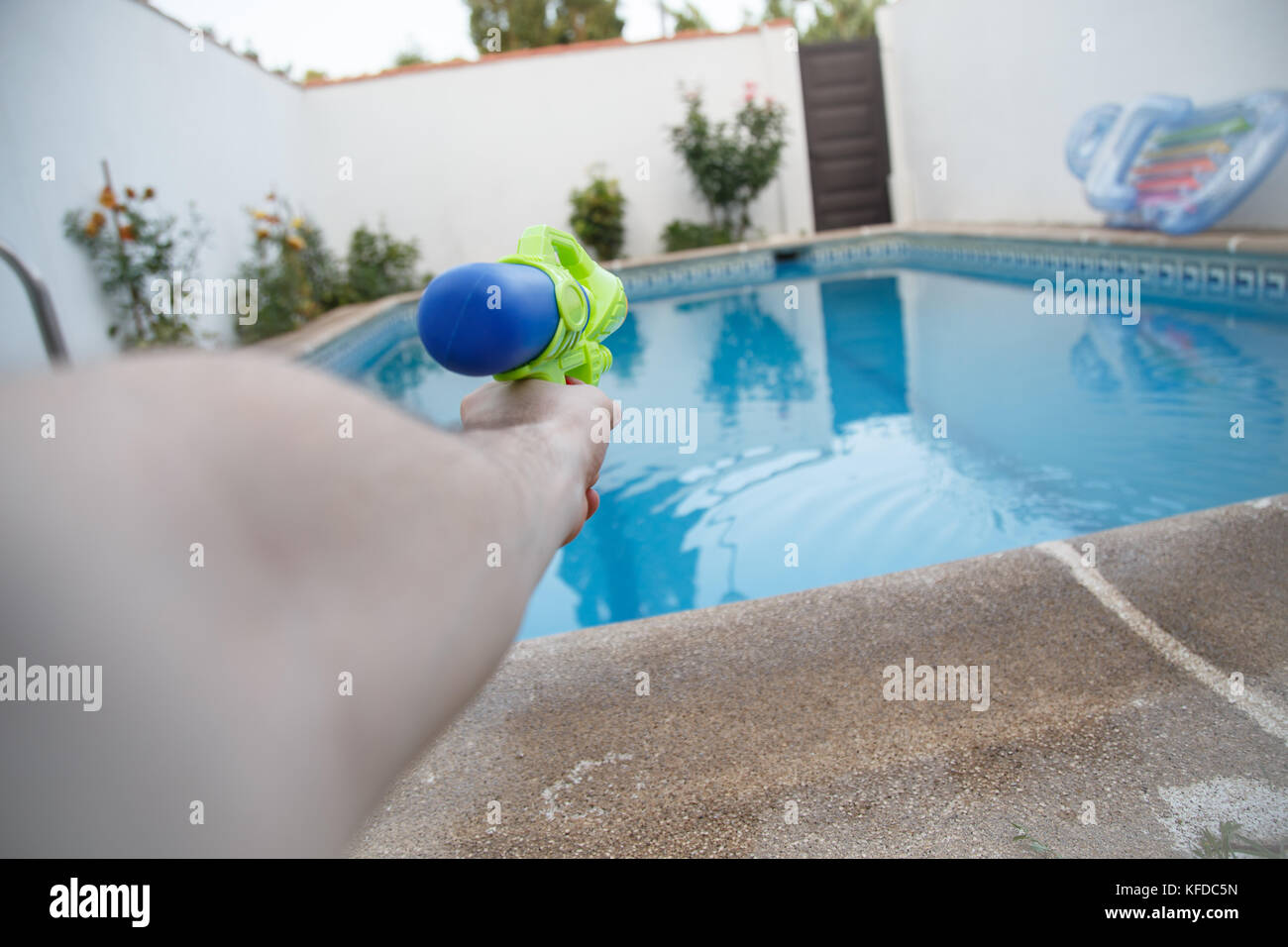 Crop shot of hand holding colorful water gun and aiming on background ...