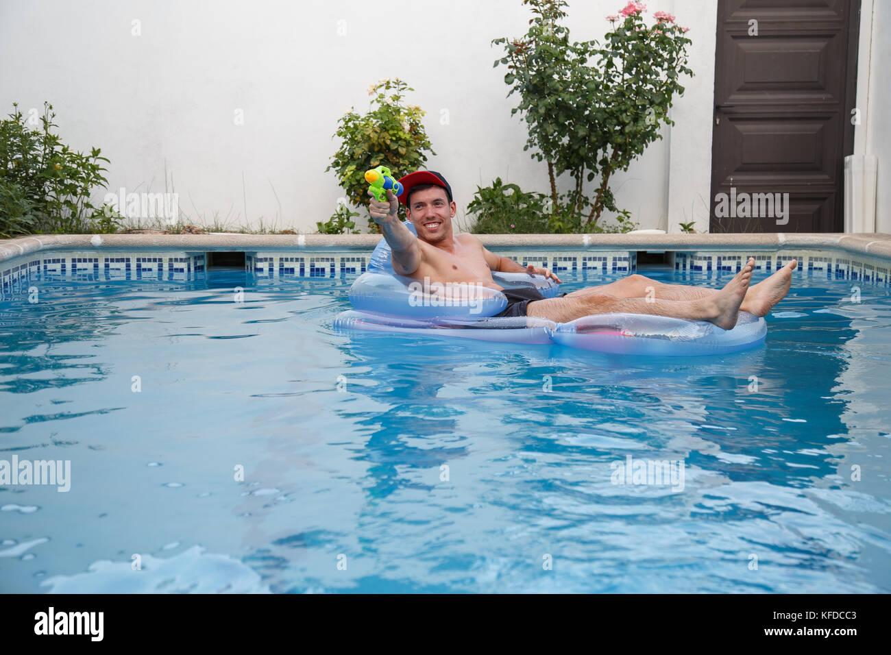 Young man sitting on inflatable and floating in pool shooting with ...