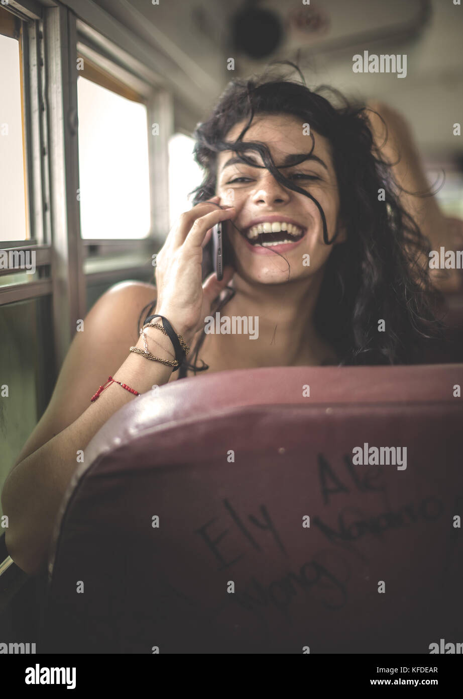 Young Woman Sitting On A School Bus Holding A Mobile Phone To Her Ear