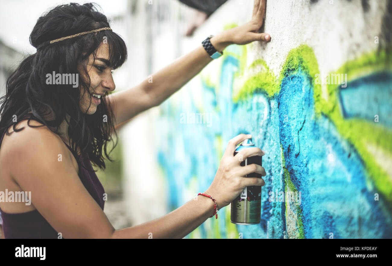 A young woman spray painting graffiti onto a wall Stock Photo - Alamy