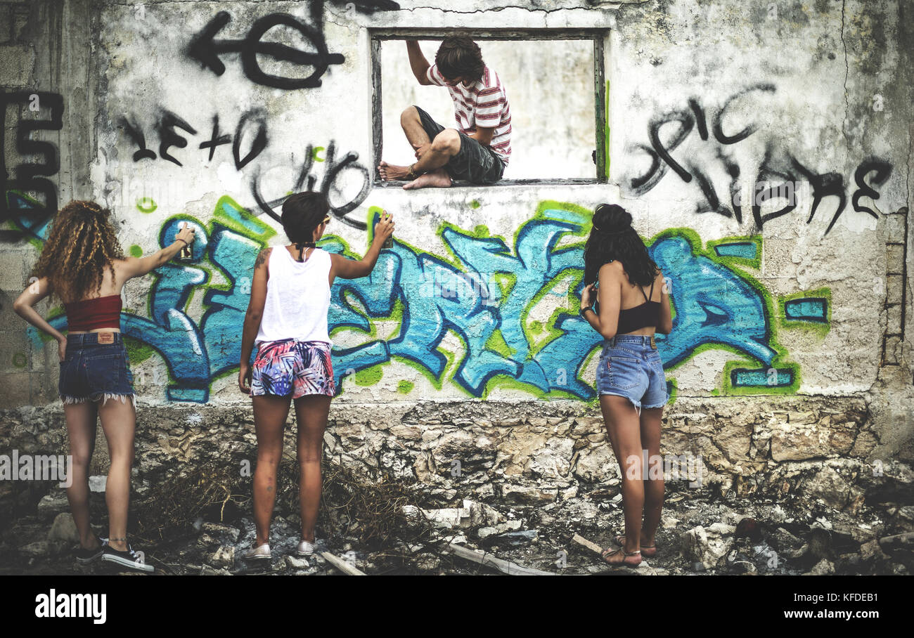 Four young people painting graffiti onto a derelict building Stock ...