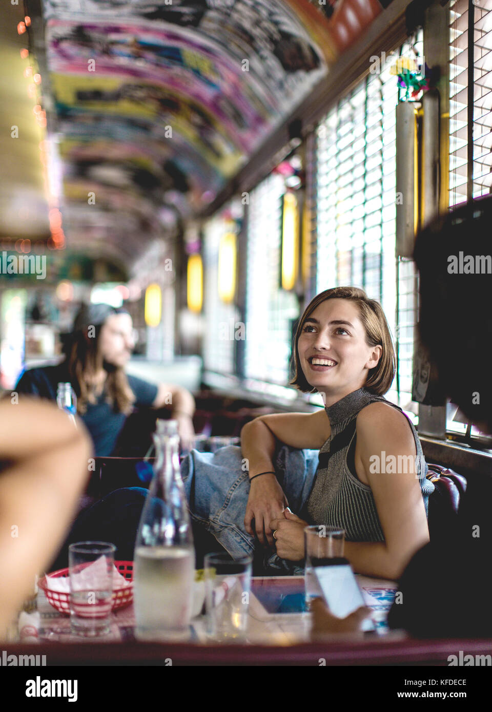 Smiling woman sitting in a booth in a diner looking up and talking to ...