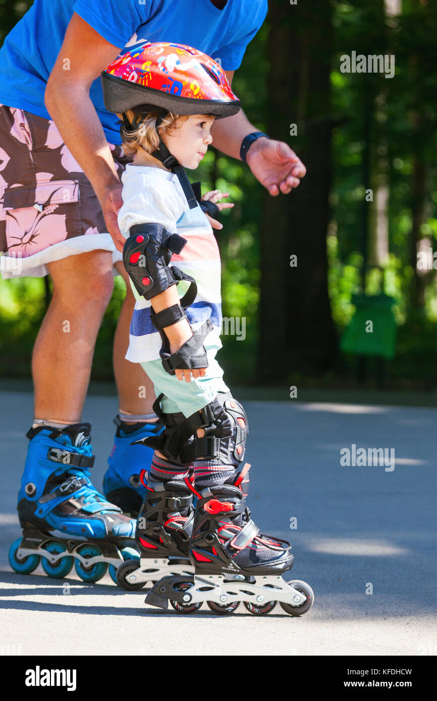 Portait of cute baby boy with inline skating instructor in the park ...