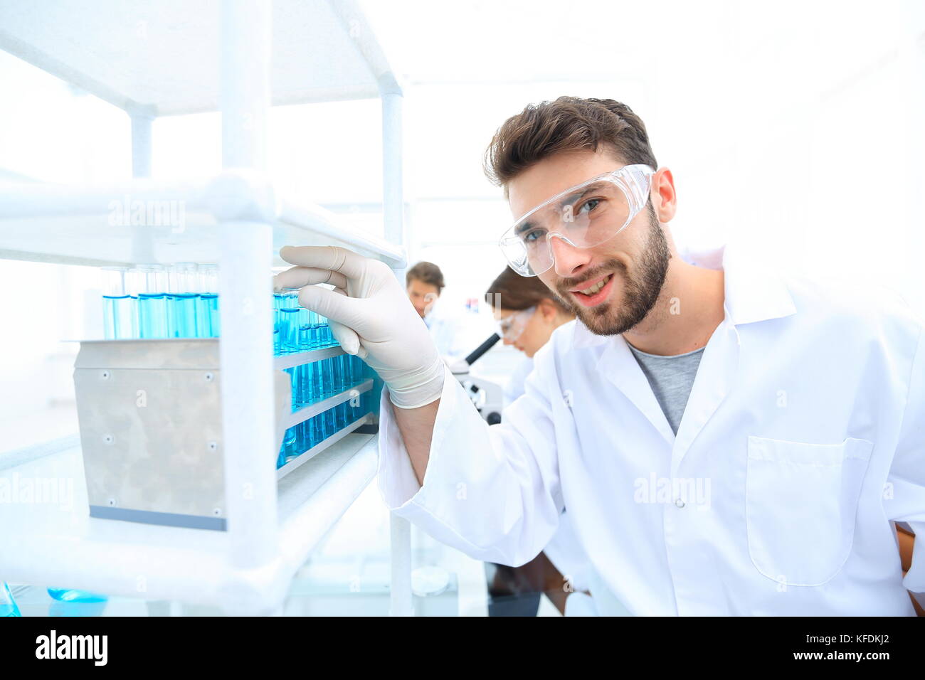 Side view of young scientist in eyeglasses looking at test tube in ...