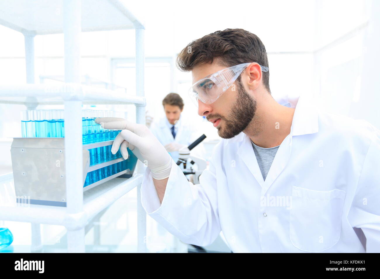 Side view of young scientist in eyeglasses looking at test tube in ...