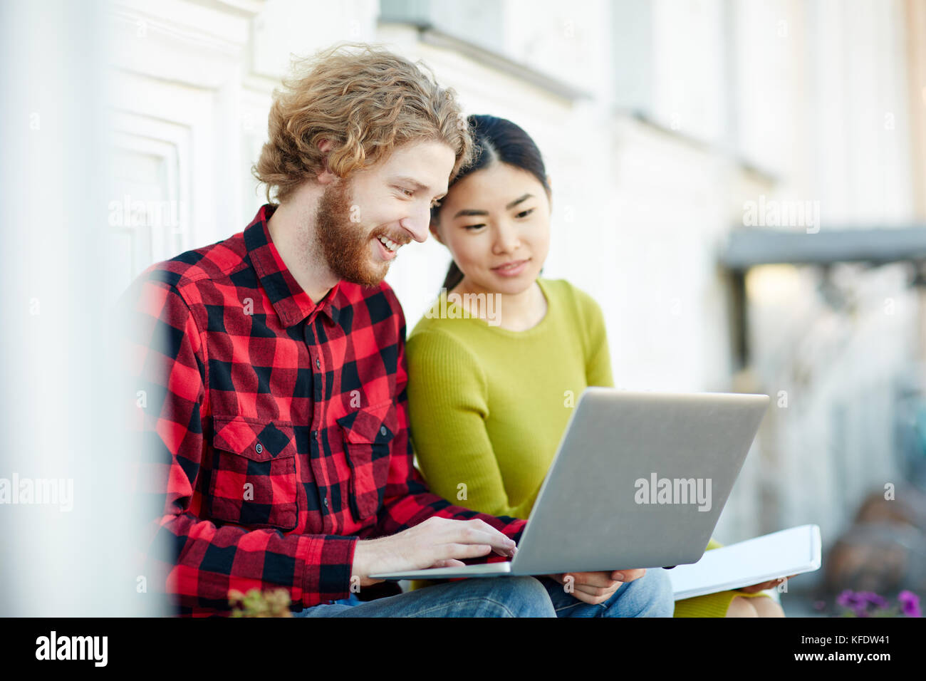 Two modern students with laptop working over college project outdoors ...