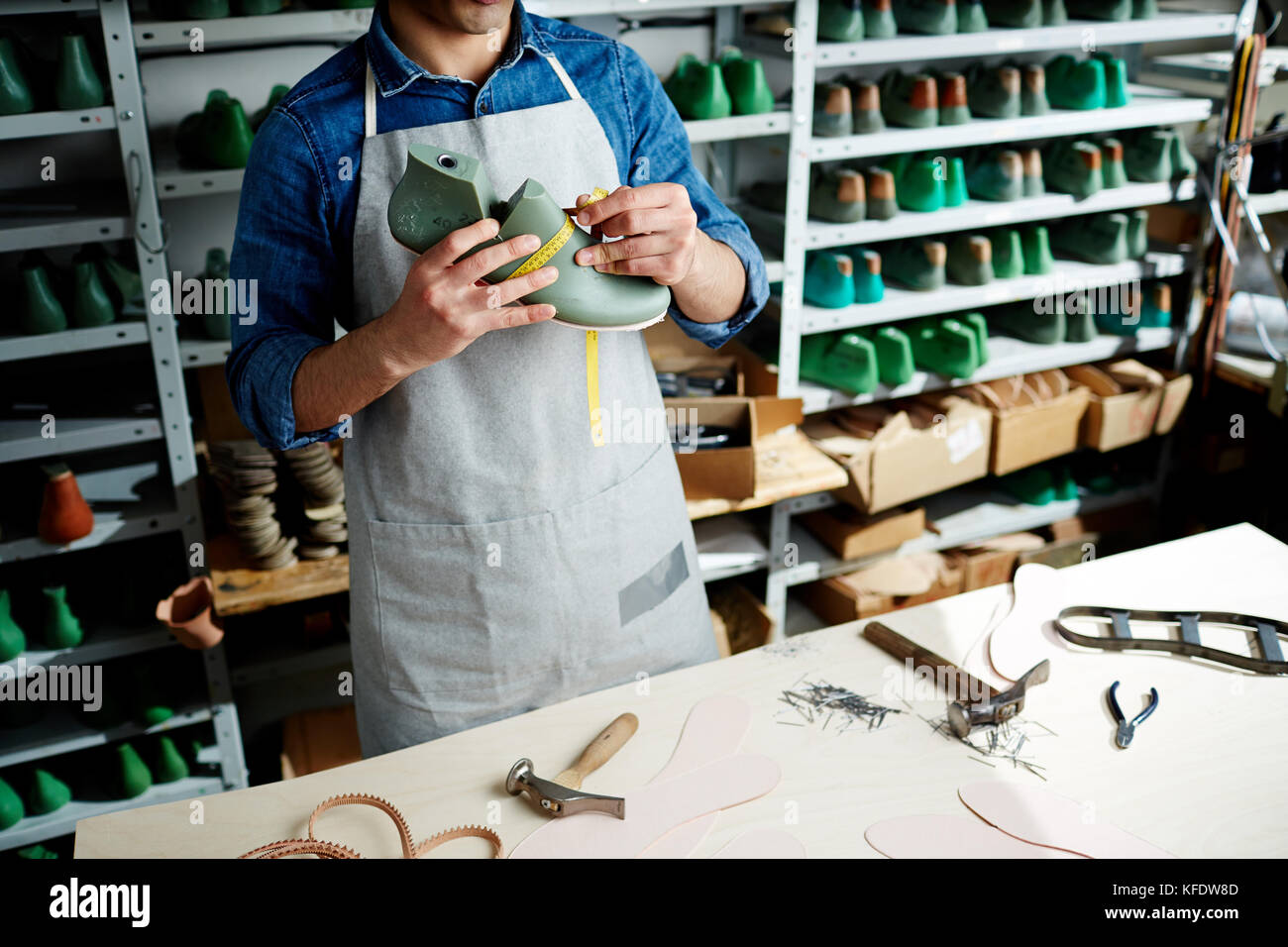 Young cobbler in uniform taking measures of shoe model over his ...