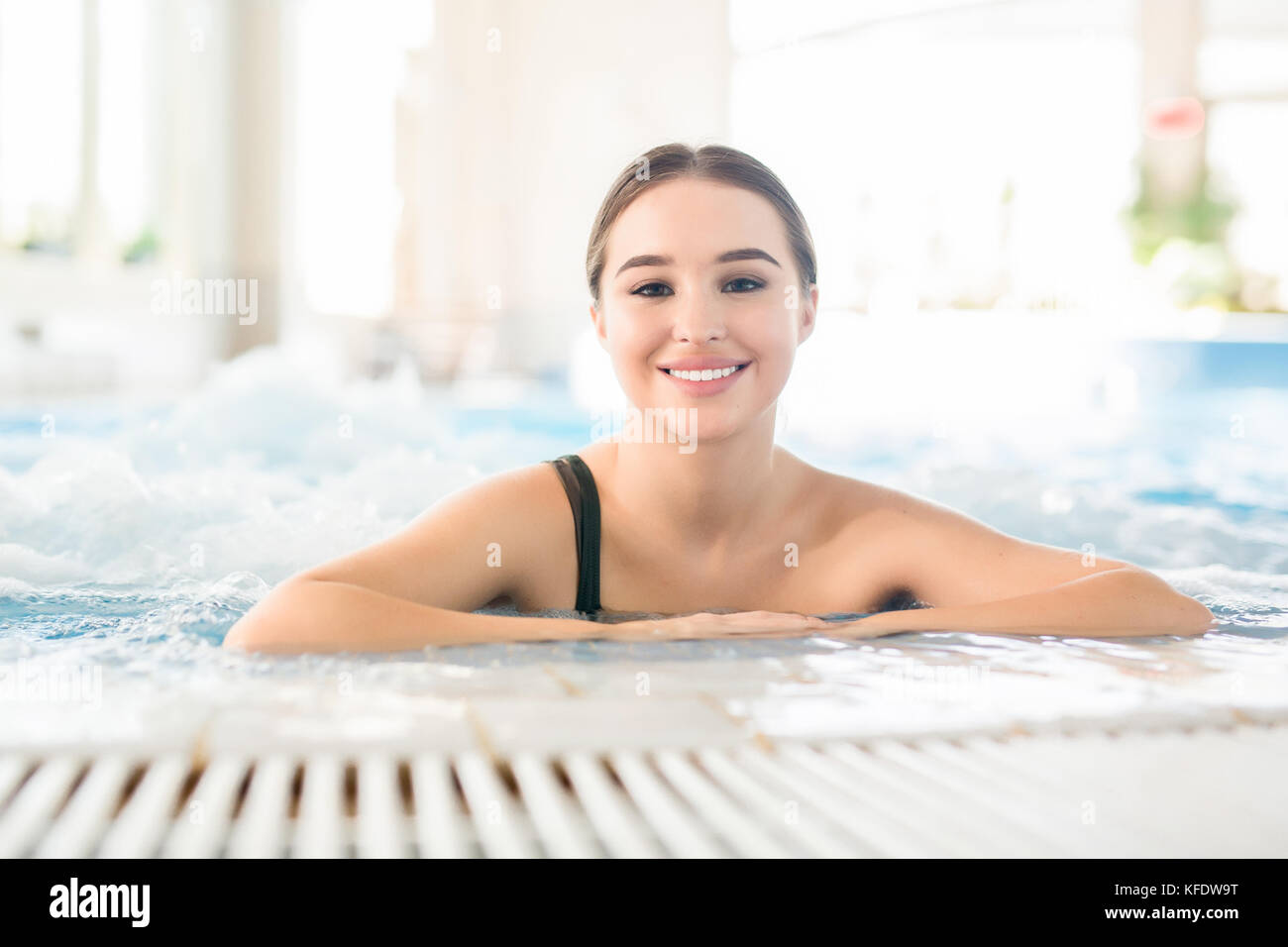 Pretty young woman with toothy smile enjoying dayspa in whirlpool with ...