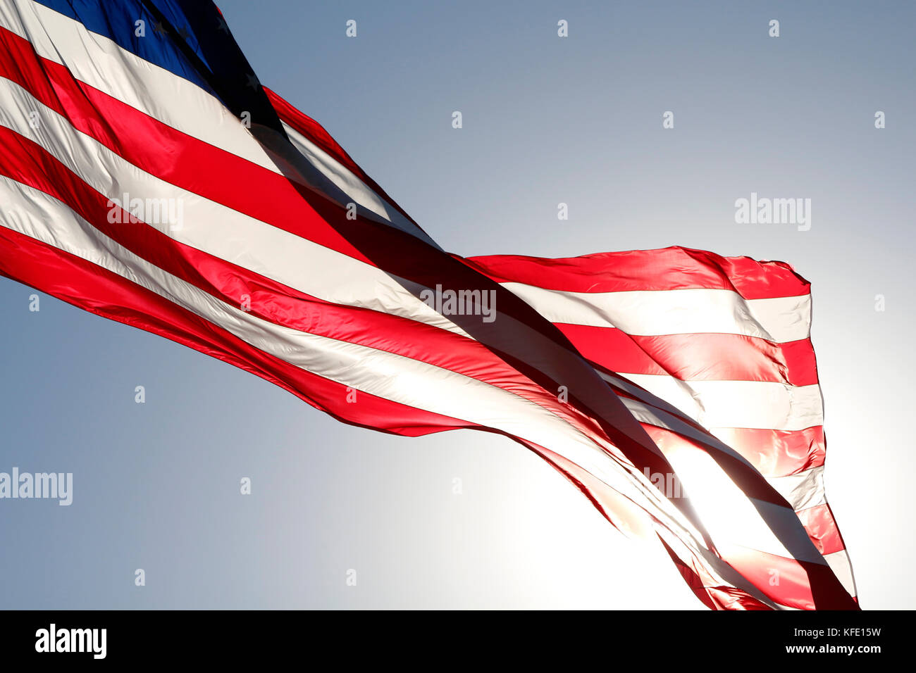 The American Flag flying proud against the sun in a clear blue sky ...