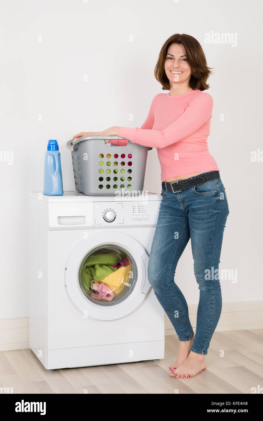 Happy Young Woman Standing By Washing Machine With Detergent And ...