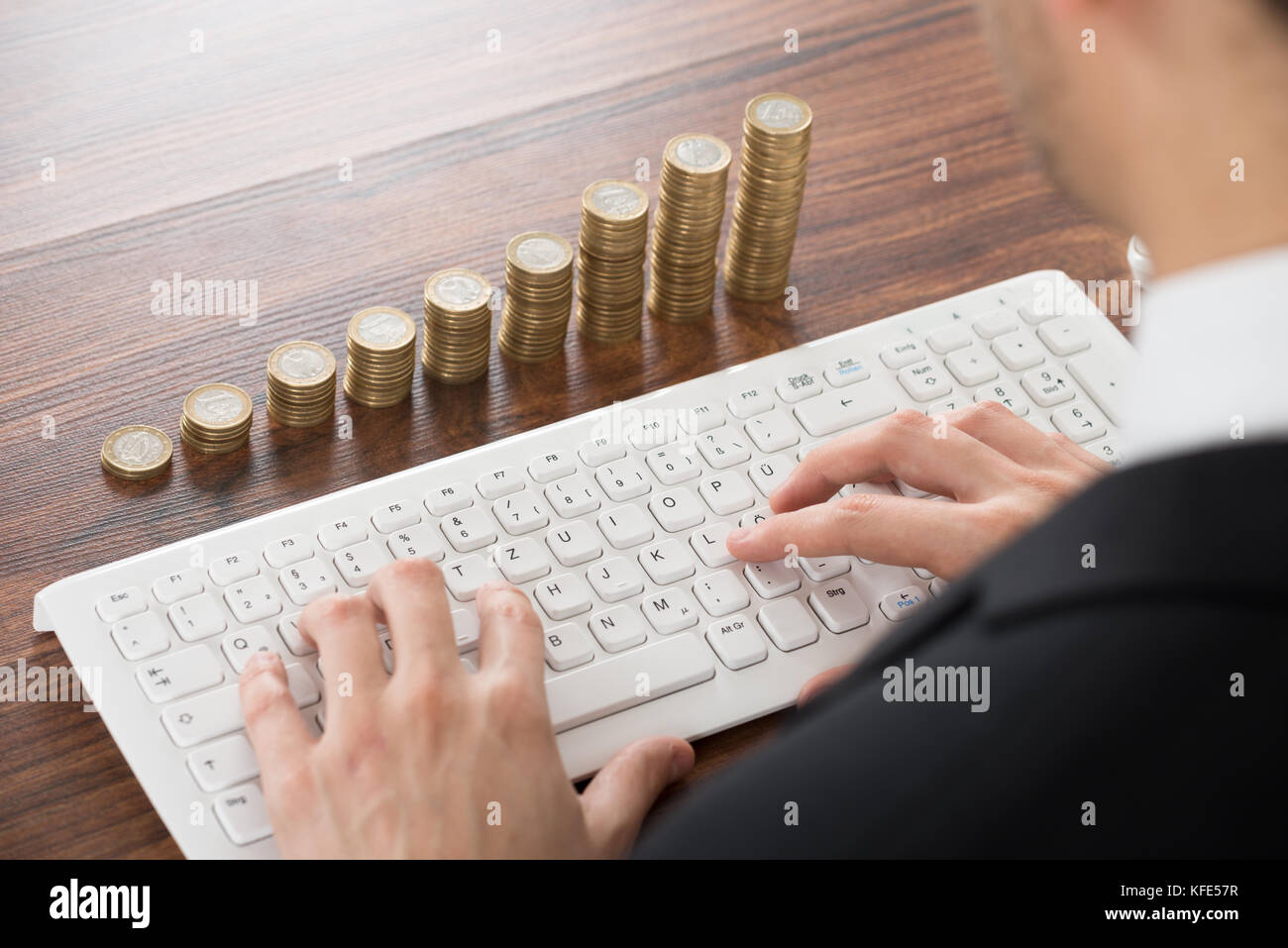 Businessman Working On Keyboard With Coins Stacked Stock Photo - Alamy