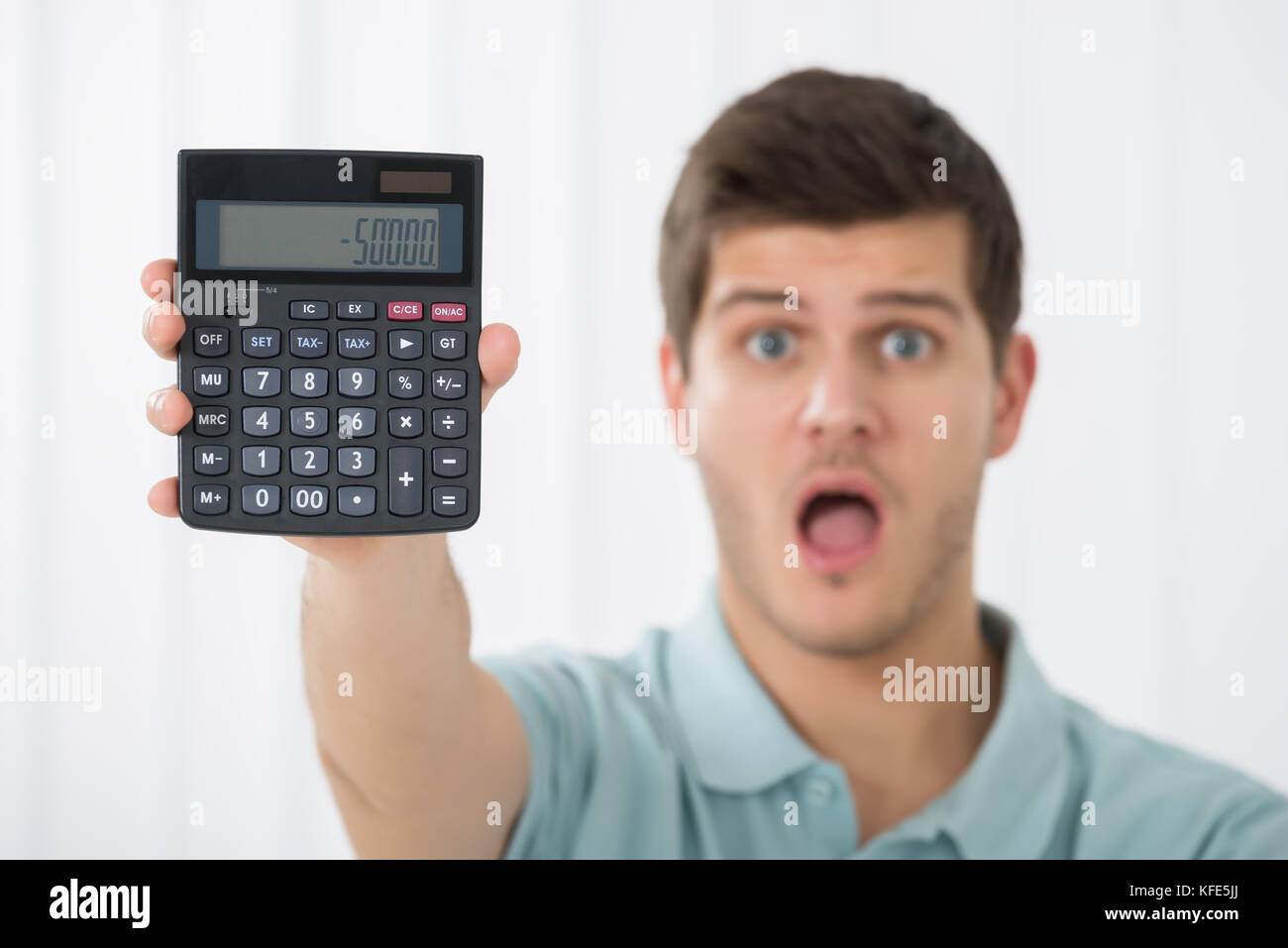 Shocked Young Man Holding Calculator At Home Stock Photo - Alamy