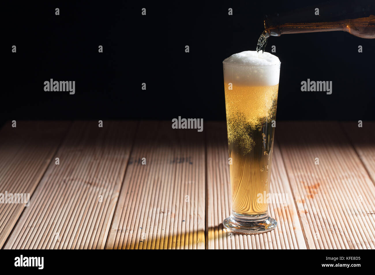 Pouring beer in a glass on a wooden table, dark background. Copy space ...