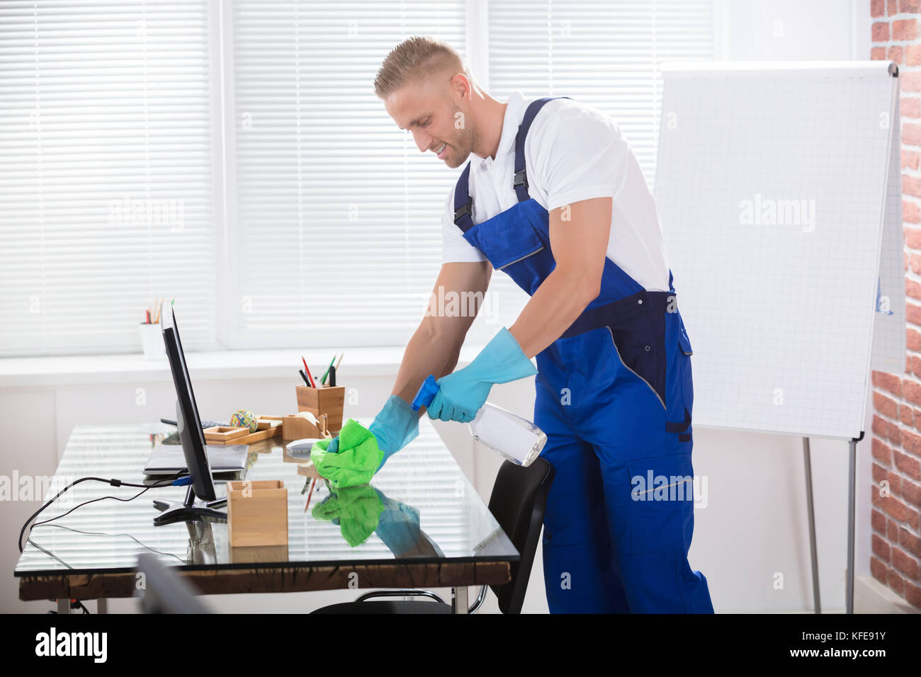 Portrait Of A Smiling Male Janitor Cleaning Desk With Cloth At ...