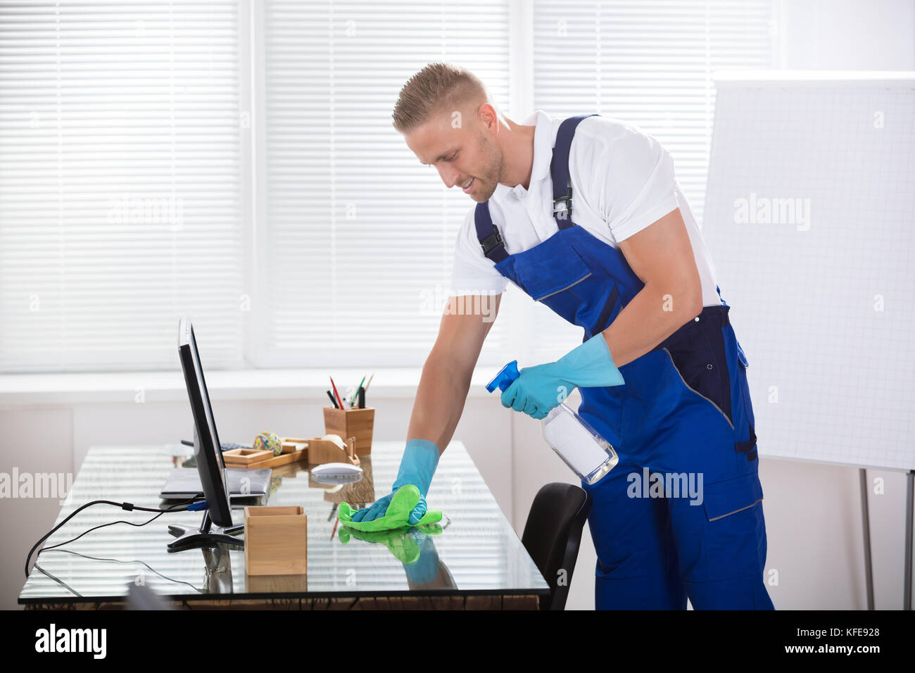 Portrait Of A Smiling Male Janitor Cleaning Desk With Cloth At ...