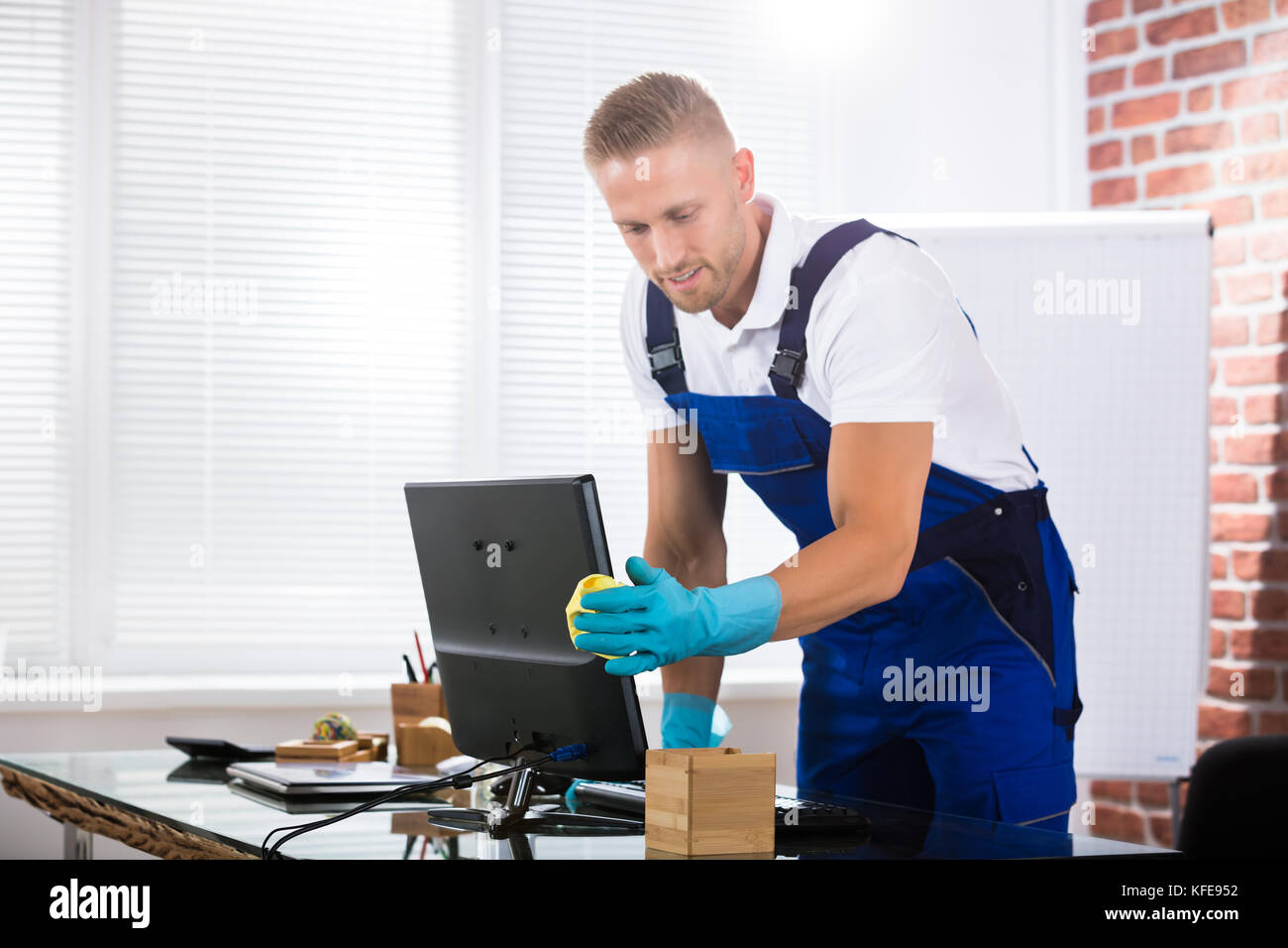 Young Male Janitor Cleaning Computer With Rag In Office Stock Photo - Alamy