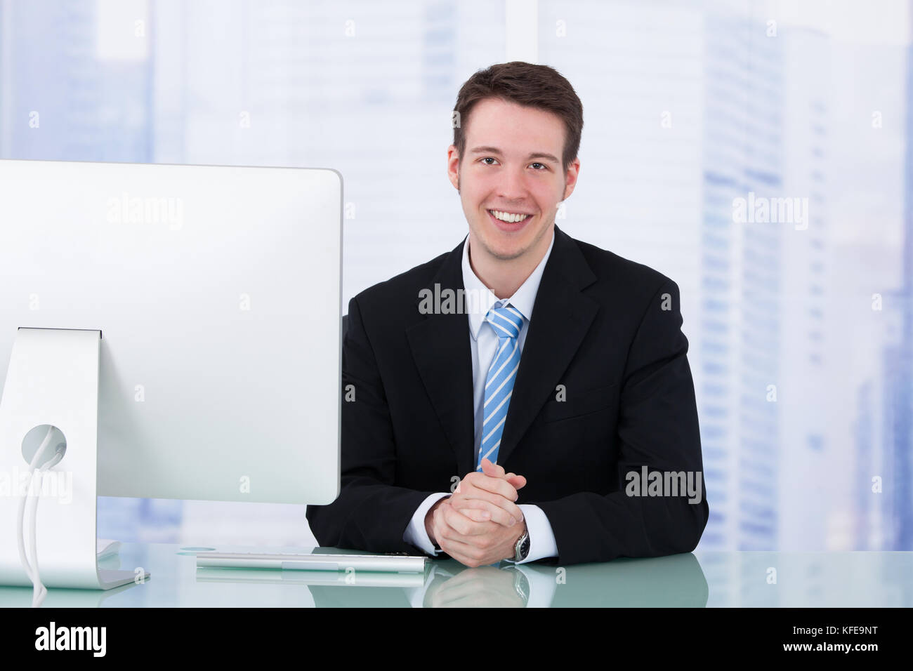 Portrait of confident young businessman using computer at office desk ...
