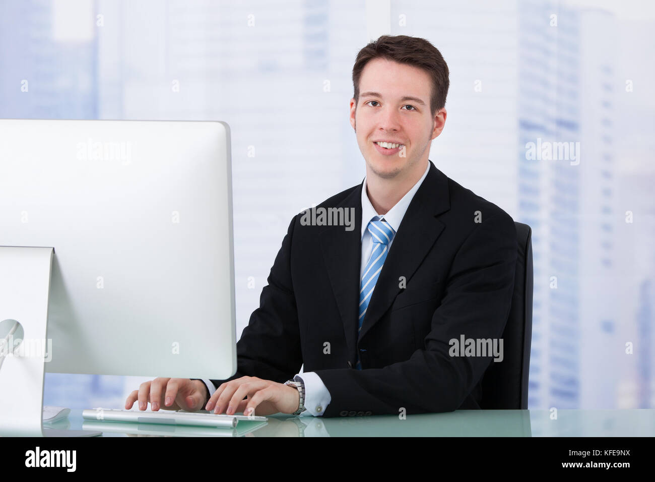 Portrait of confident young businessman using computer at office desk ...