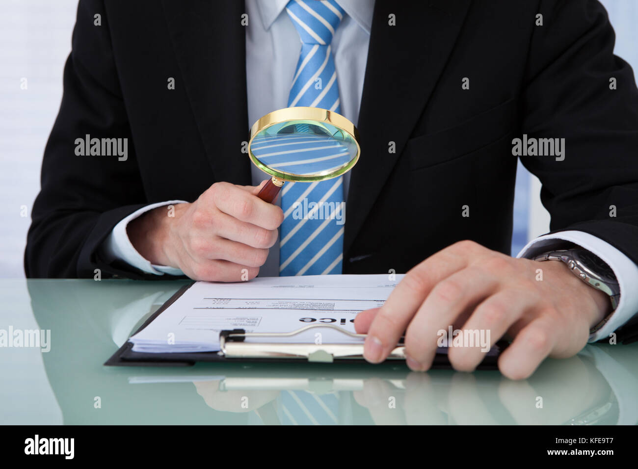 Midsection of young businessman examining invoice through magnifying ...