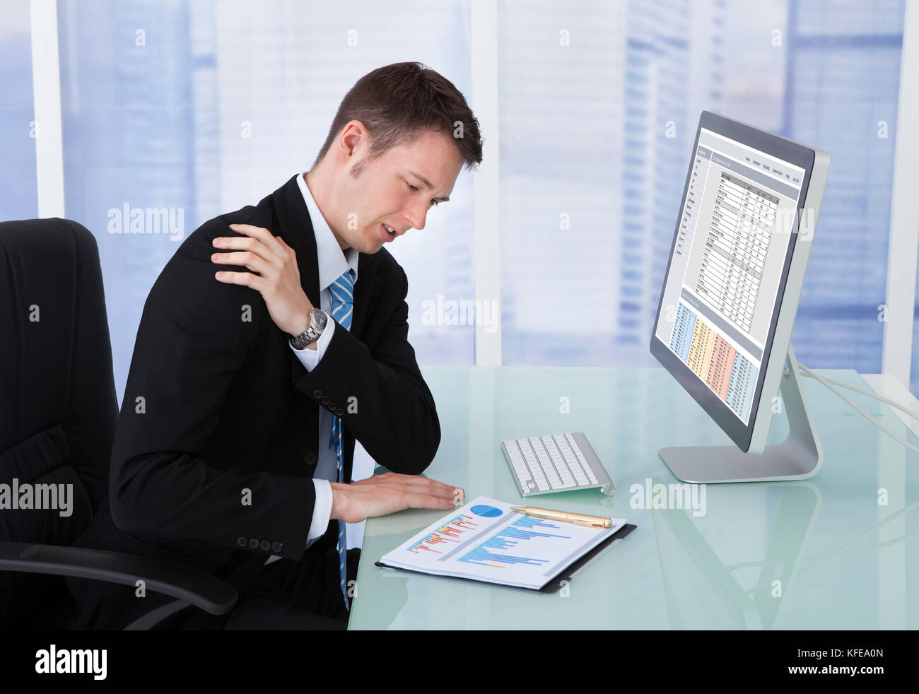 Young businessman having shoulder pain while working at computer desk ...