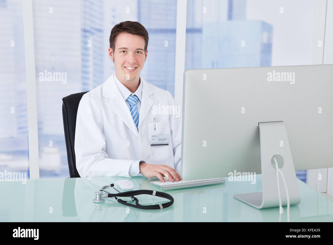 Portrait of confident young male doctor using computer at desk in ...