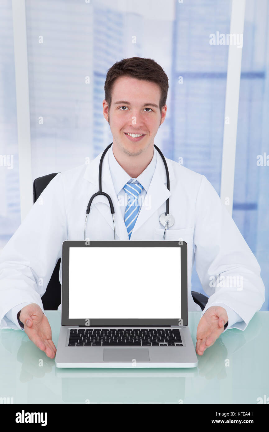 Portrait of confident young male doctor presenting laptop with blank ...