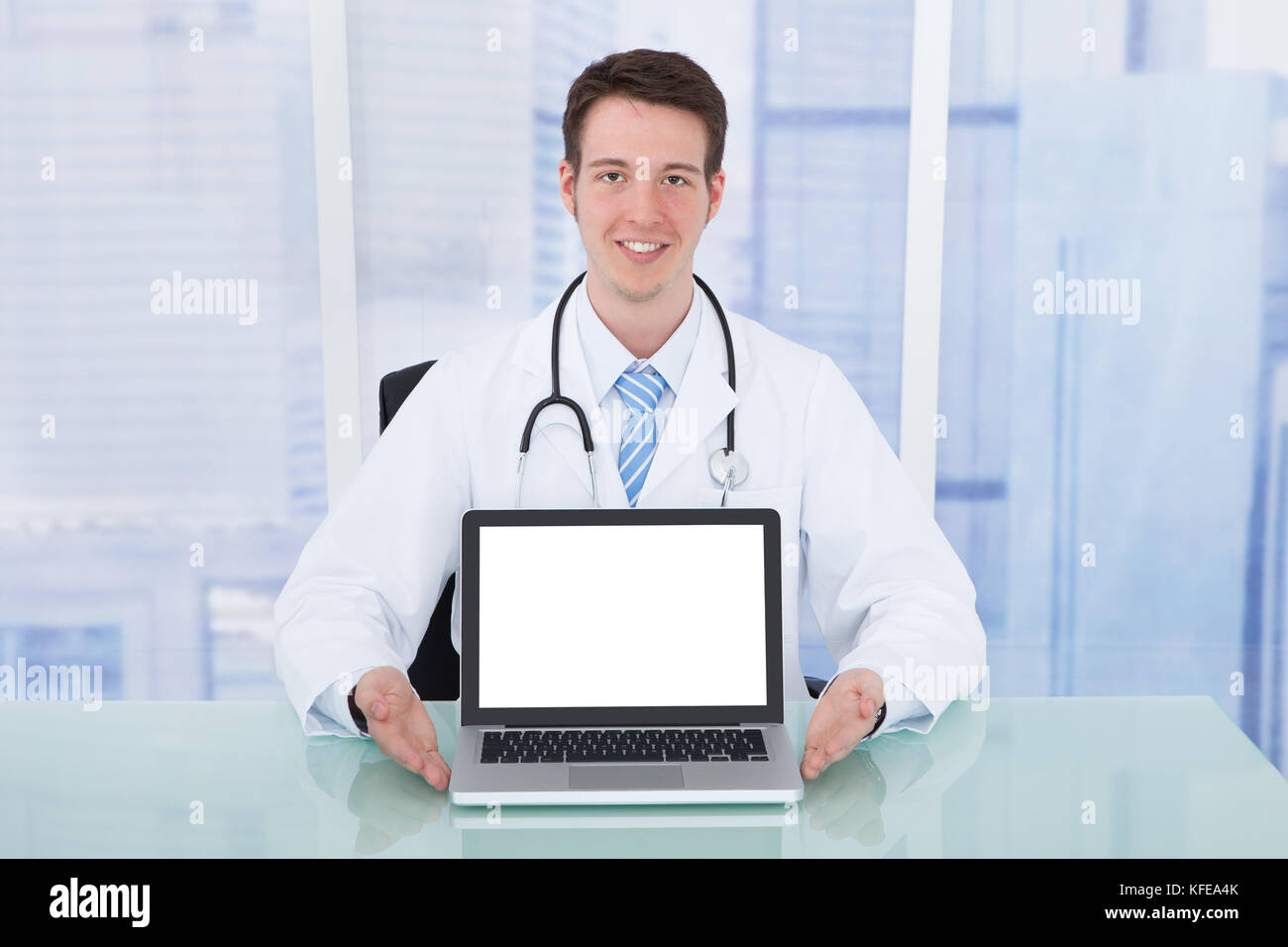 Portrait of confident young male doctor presenting laptop with blank ...