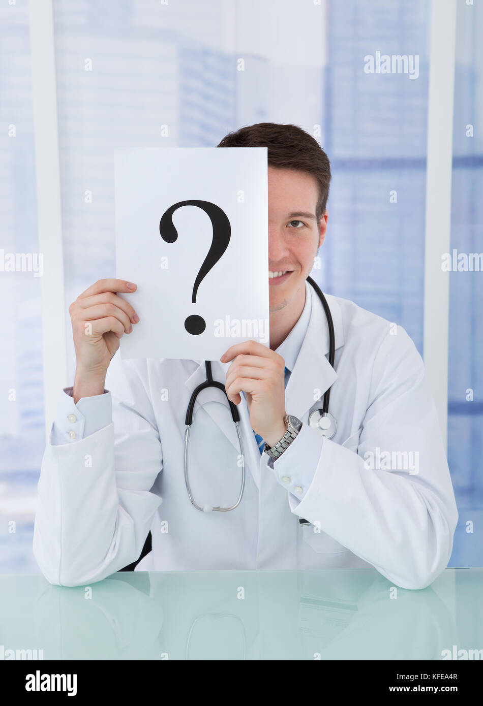 Portrait of smiling young doctor holding paper with question mark at ...