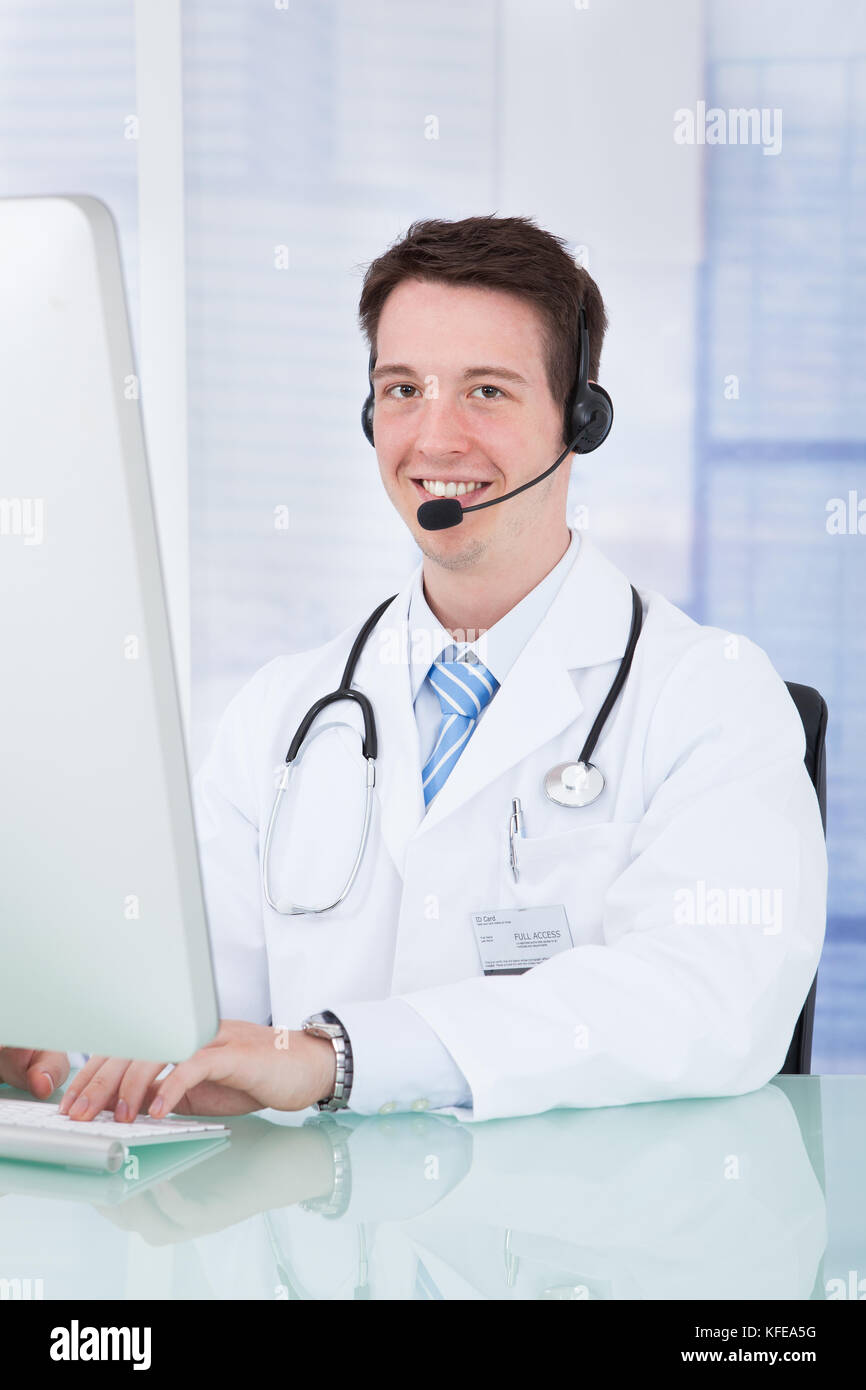 Portrait of young male doctor wearing headset while using computer at ...