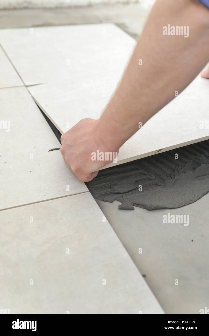 Man placing ceramic floor tile in position over adhesive Stock Photo ...