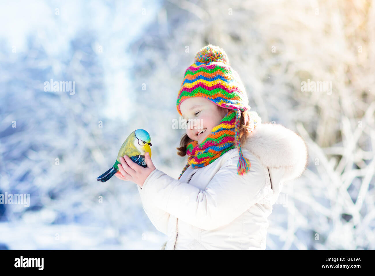 Child feeding tit bird in winter park. Kids feed birds in snowy forest ...