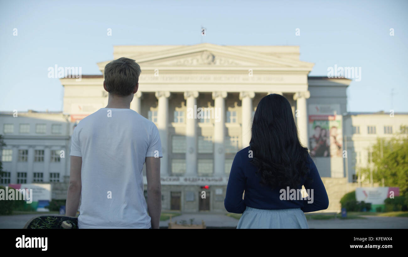 Rear view portrait of two students carrying walking and look at the ...