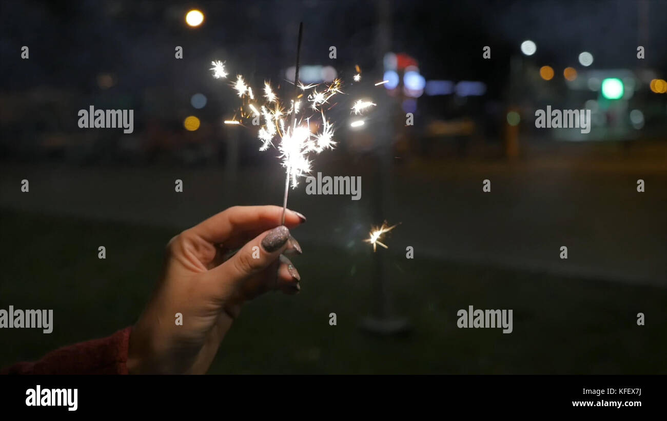 Female hand holding sparklers in the street. Close up of woman holding ...